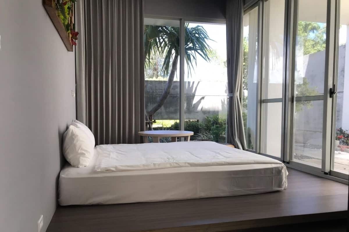 Quarto com uma cama, uma mesa redonda pequena e vista para o exterior através de janelas amplas.