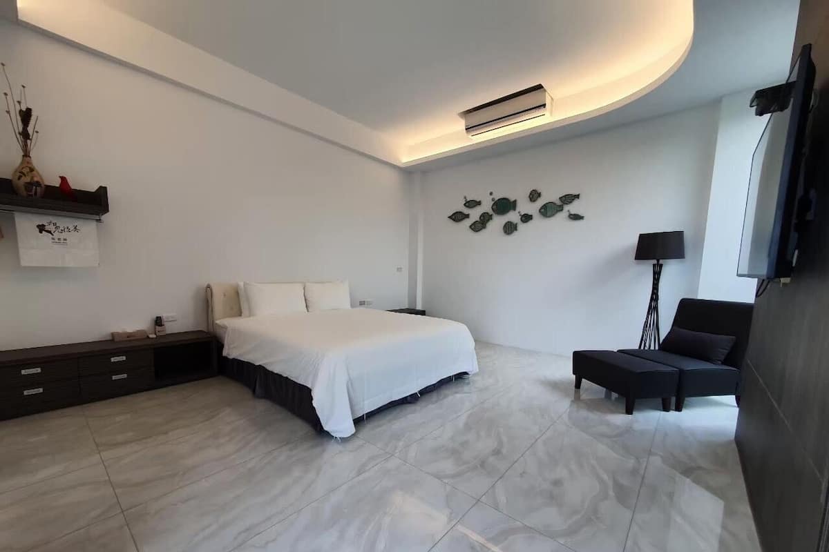 Quarto moderno com uma cama grande, uma mesa de cabeceira, uma cadeira e uma televisão.