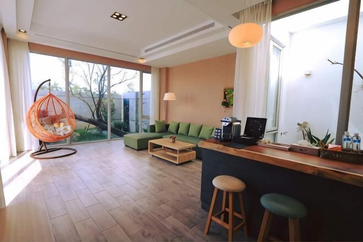 Uma sala de estar moderna com sofá, cadeira suspensa, mesa de centro e área de bar com bancos.