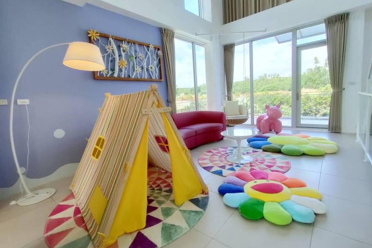 Quarto espaçoso com área de recreação, incluindo uma tenda, almofadas de diversos colores e um sofá vermelho.
