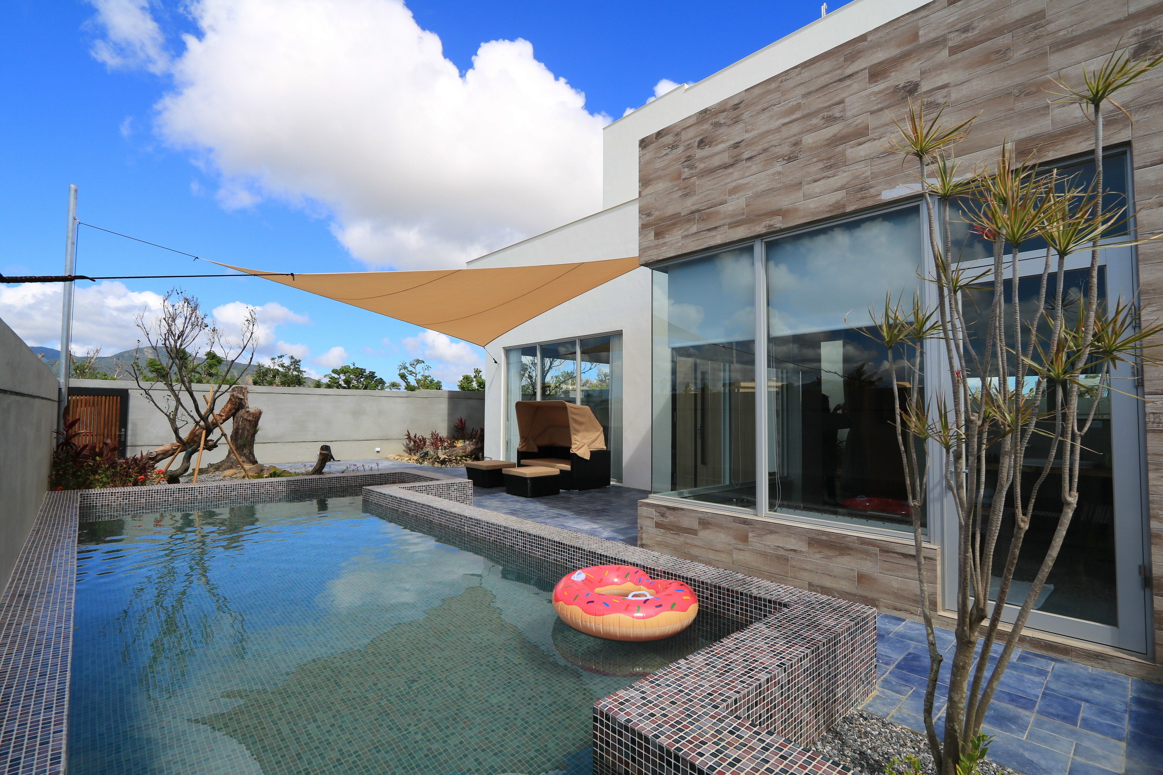 Uma área de piscina moderna ao ar livre, com estrutura de vidro, espreguiçadeira e toldo.