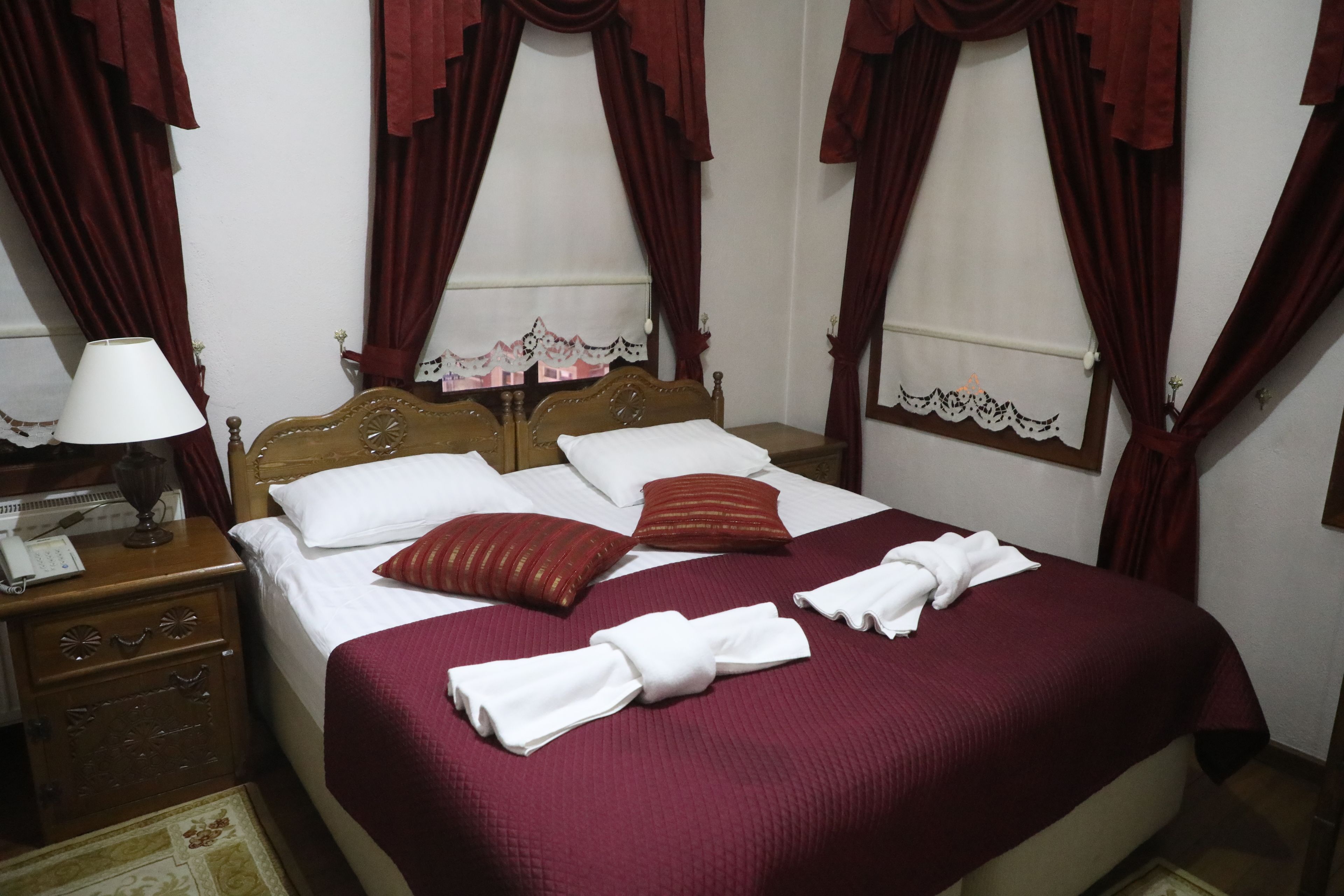 Cama bem arrumada com roupa de cama branca e vermelha, cabeceira de madeira e cortinas vermelhas.