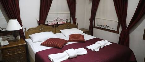 Cama bem arrumada com roupa de cama branca e vermelha, cabeceira de madeira e cortinas vermelhas.