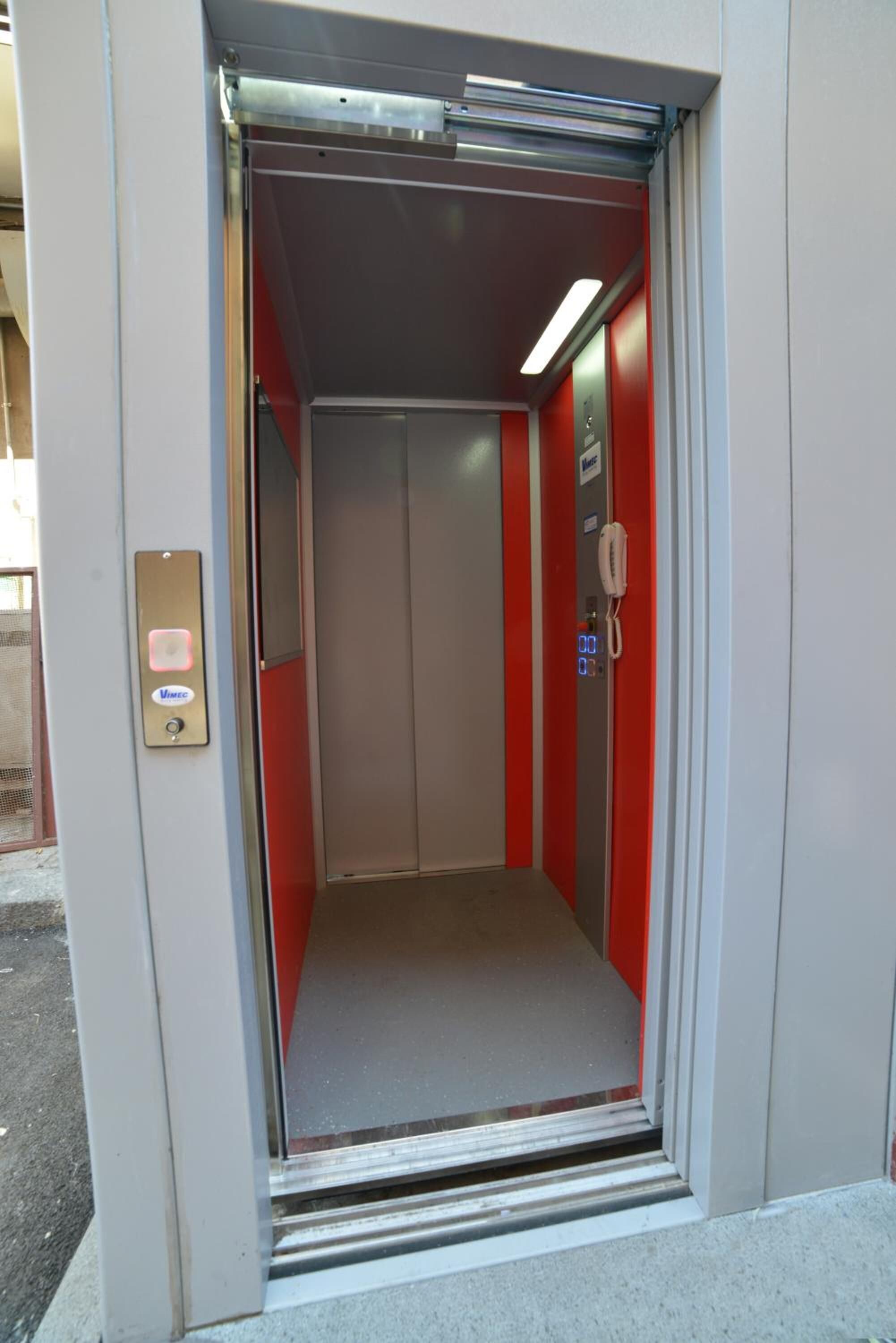 Um elevador com painel de controle, paredes vermelhas e porta de metal.