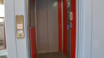Um elevador com painel de controle, paredes vermelhas e porta de metal.