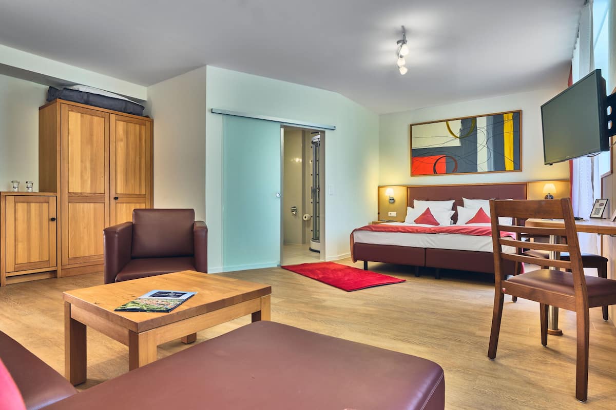 Quarto de hotel com cama, escrivaninha, cadeira, sofá, mesa de centro, guarda-roupa e televisão.
