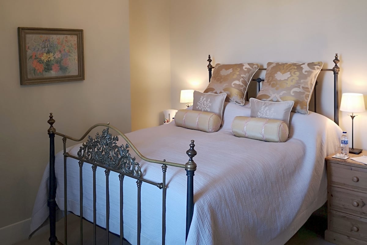 Quarto com cama, mesas de cabeceira, um candelabro e uma obra de arte floral emoldurada na parede.
