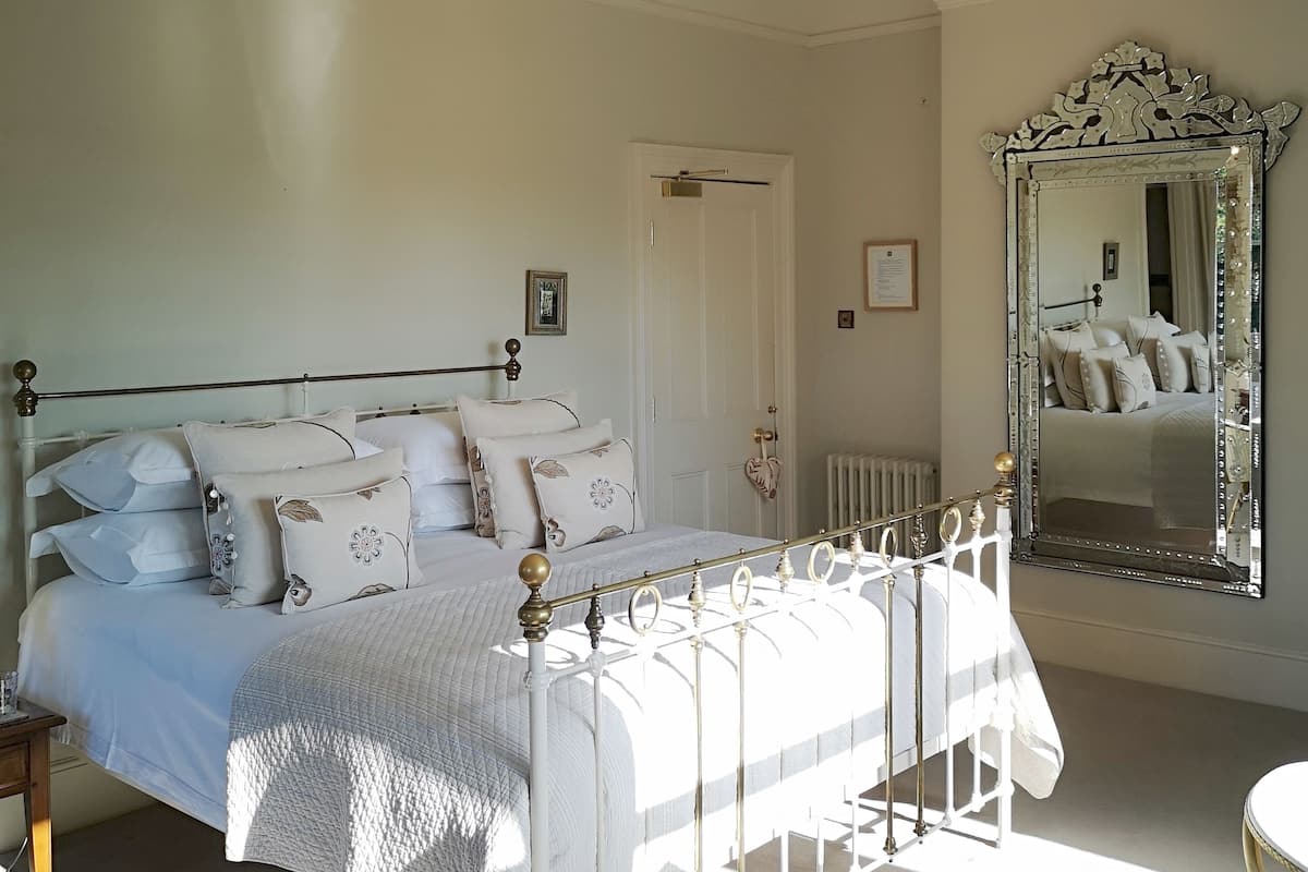 Um quarto com uma cama branca, um candelabro, um espelho grande e uma porta.