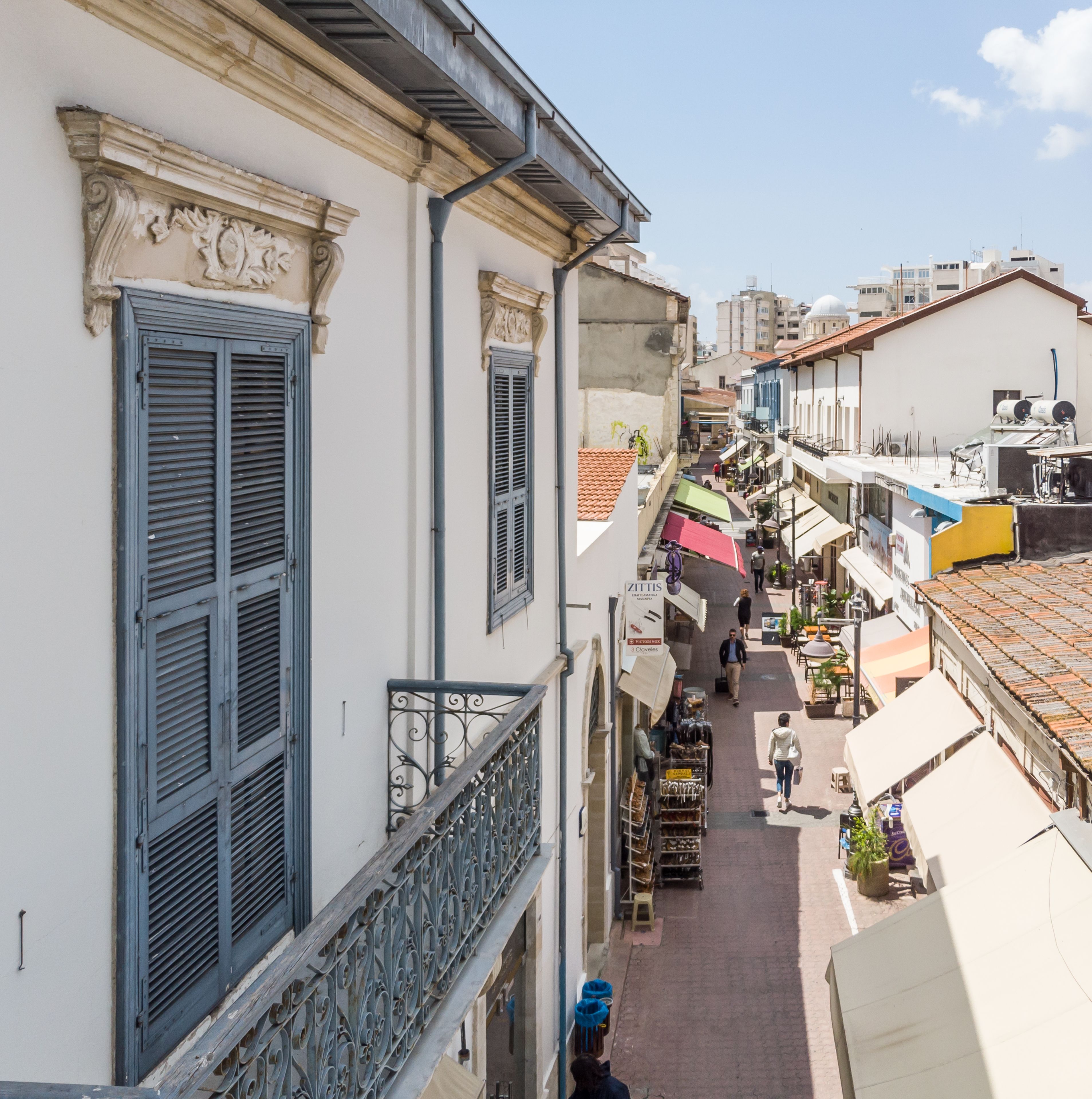 Uma rua estreita ladeada por edifícios, com varandas e treliças de metal e persianas.