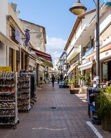 Rua estreita com lojas e um quiosque que vende sandálias.