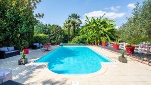 Piscina retangular com deck revestido, rodeada por plantas em vasos e móveis de exterior.