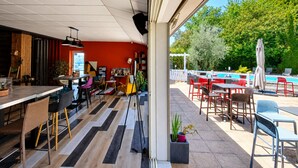 Uma área de refeições interna moderna com vista para a piscina, apresentando diferentes opções de assento e uma piscina ao ar livre visível.