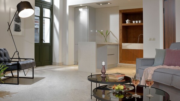 Uma sala de estar moderna com sofá, uma mesa de centro de vidro com livros e taça de vinho, um abajur e uma estante.
