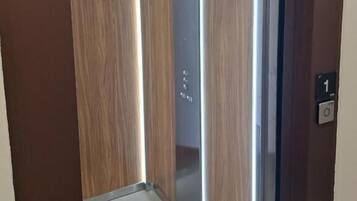 Elevador com acabamento em madeira e painel de controle com um botão marcado '1'.