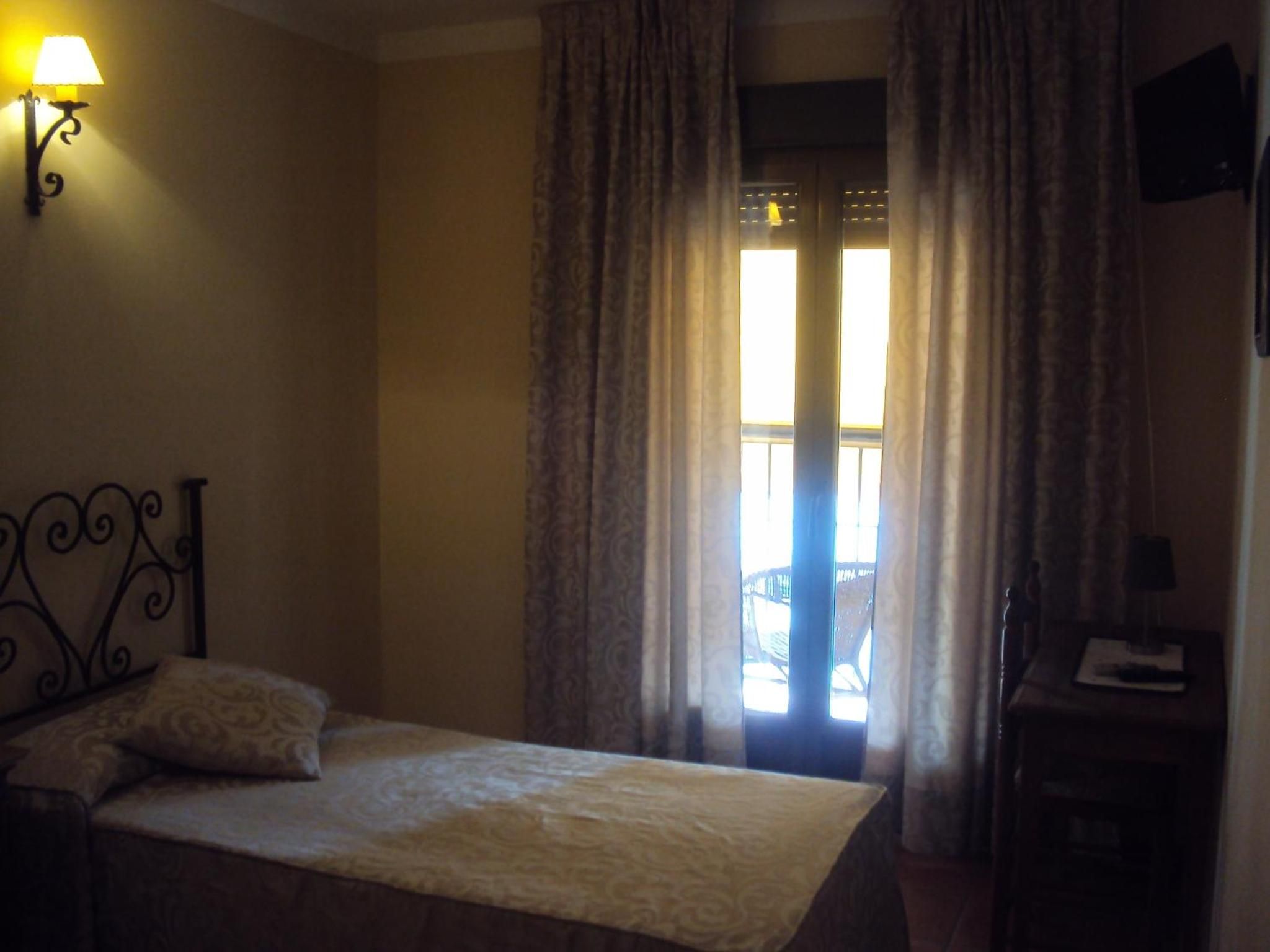 Quarto com cama, mesa de cabeceira, luminária e janela com cortinas.