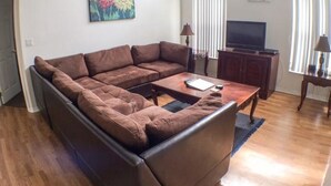 Uma sala de estar com sofá seccional, mesa de centro, televisão e obras de arte nas paredes.