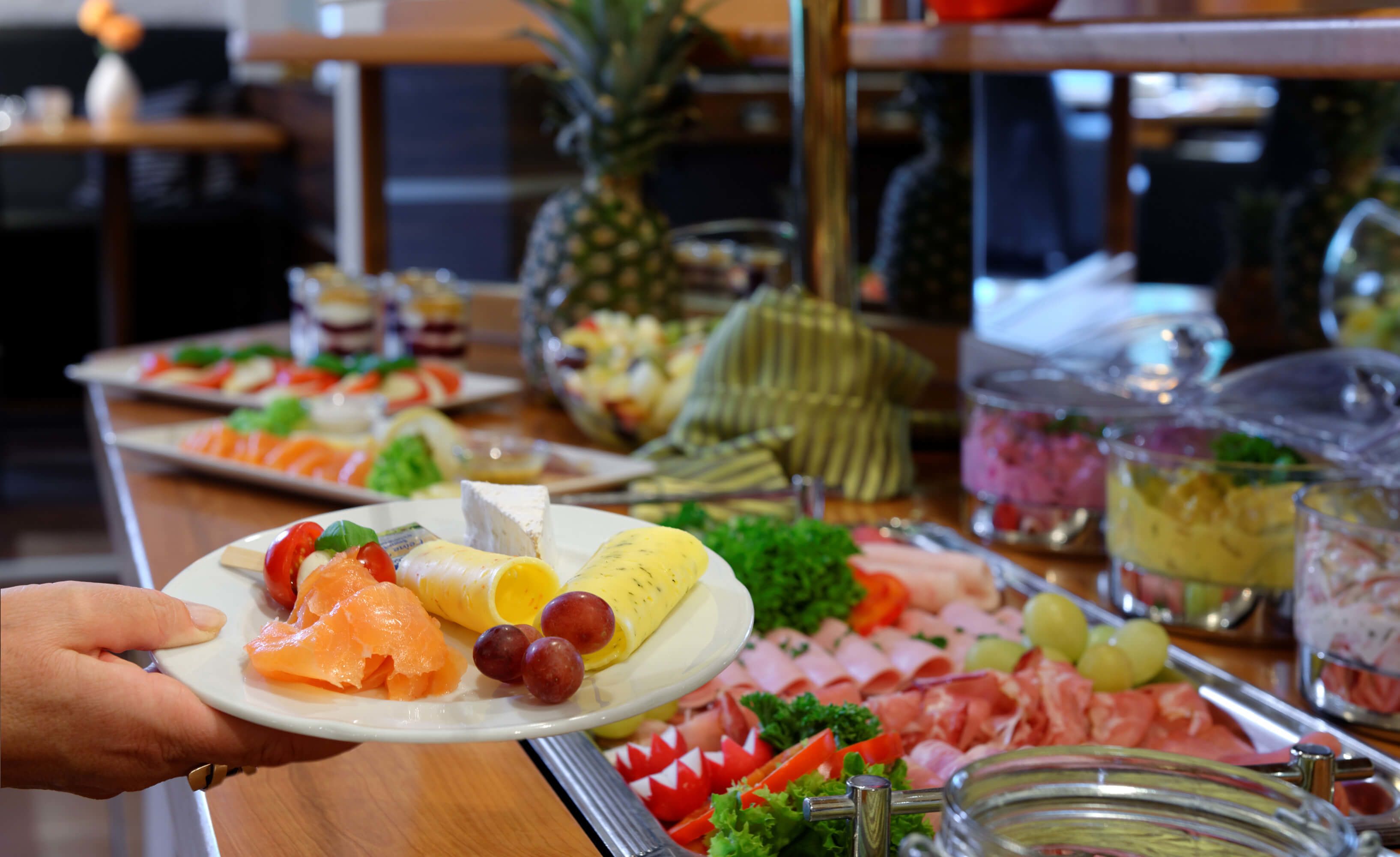 Mesa de buffet com diversos alimentos, incluindo salmão defumado, queijos e frutas.