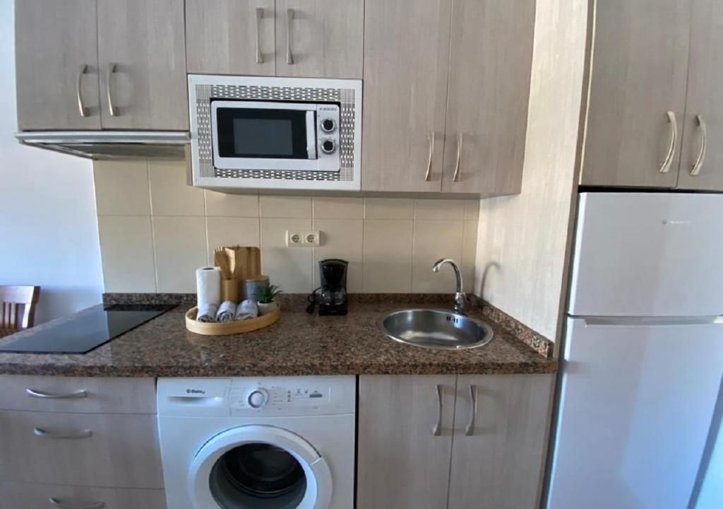Cozinha compacta com micro-ondas, cafeteira, pia e máquina de lavar roupa.