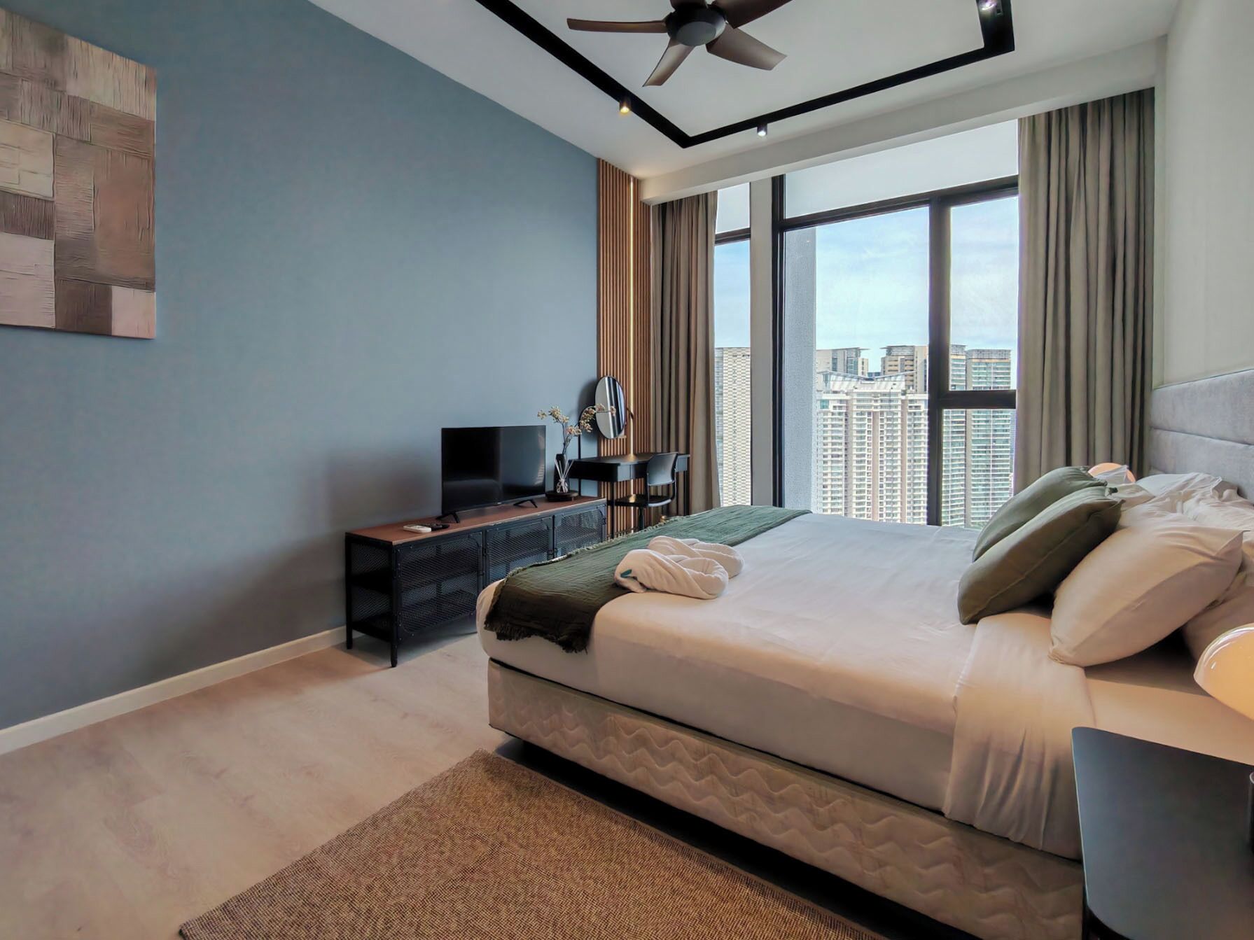 Quarto moderno com cama, televisão, escrivaninha e uma grande janela com vista para a cidade.