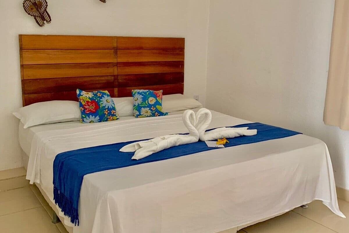 Cama bem arrumada com manta azul e toalha branca disposta em formato de cisne.