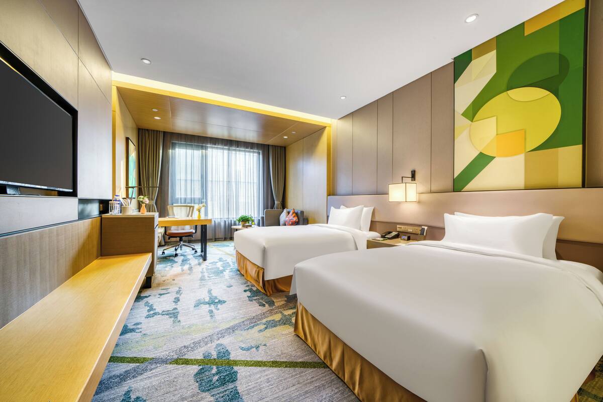 Quarto de hotel com duas camas, uma escrivaninha, televisão e um grande quadro abstrato na parede.