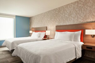 Quarto de hotel com duas camas, uma janela grande e parede estampada.