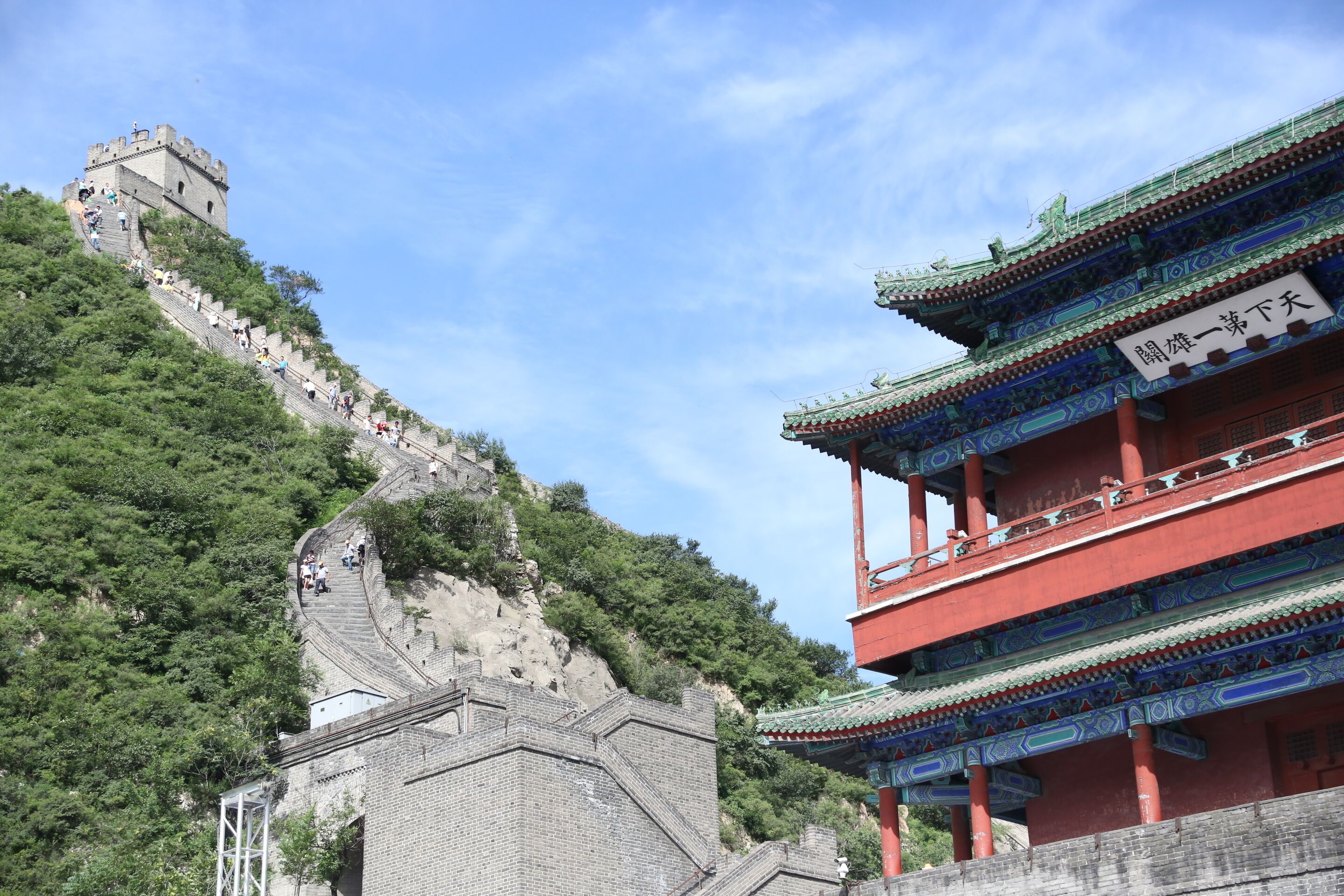 Um edifício tradicional chinês com telhado vermelho e verde, ao lado de uma escadaria de pedra que sobe uma colina.
