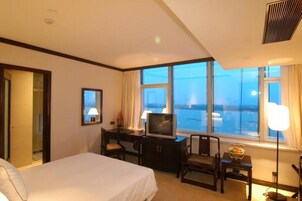 Quarto de hotel com uma cama grande, uma escrivaninha com computador, uma cadeira e vista para a água.