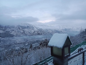 Paisagem coberta de neve com vista para montanhas distantes e uma cerca verde.