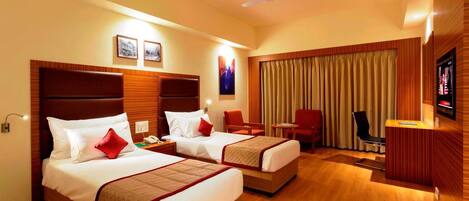 Quarto de hotel com duas camas, uma escrivaninha, uma cadeira, televisão e ventoinha no teto.