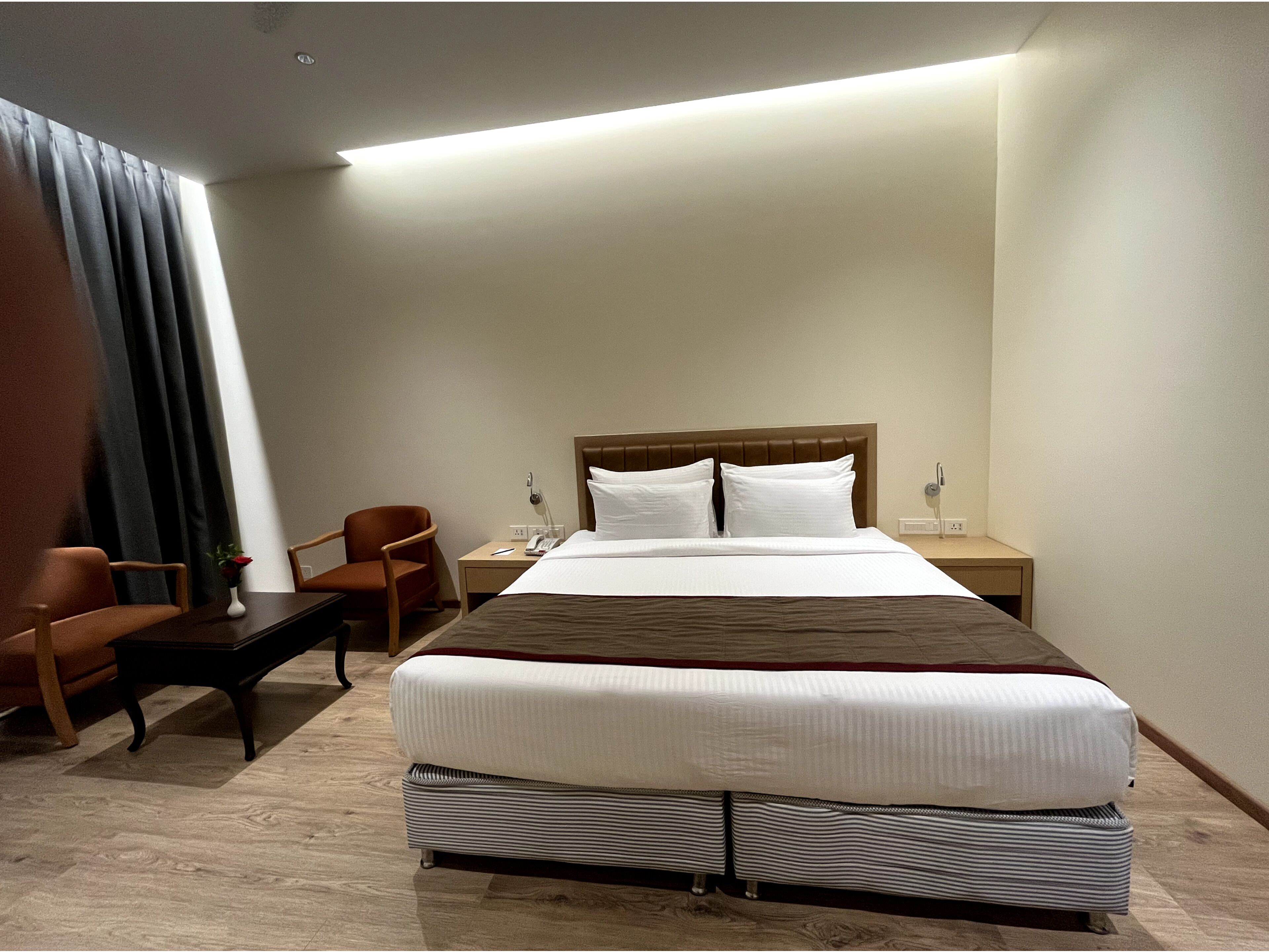 Quarto de hotel com uma cama grande, mesa de cabeceira, uma cadeira e uma escrivaninha.