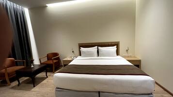 Quarto de hotel com uma cama grande, mesa de cabeceira, uma cadeira e uma escrivaninha.