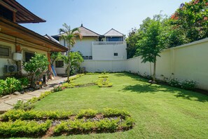 Um jardim bem cuidado, com gramado, um caminho e um edifício branco com telhado em telhas.