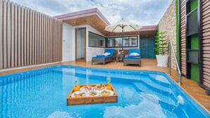Uma área de piscina moderna com deck de madeira, espreguiçadeiras e uma bandeja de comida.