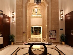 Um hall de hotel com piso de mármore, balcão de recepção e um lustre.