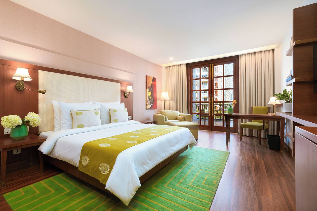 Quarto de hotel com uma cama grande, uma escrivaninha, uma cadeira e vista da cidade pela janela.