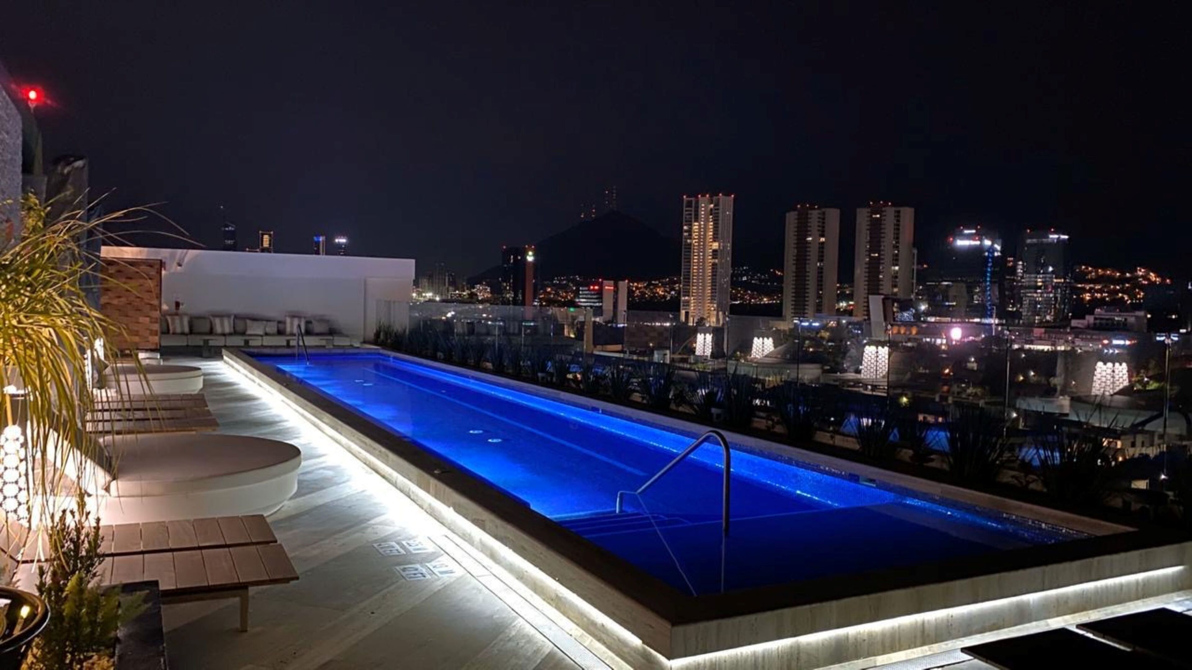 Piscina no terraço com vista para a cidade, área de estar e mesa à beira da piscina.
