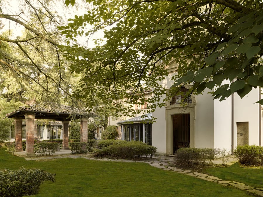 Um jardim bem cuidado com um gazebo, um edifício branco com varanda coberta e um caminho de pedra.