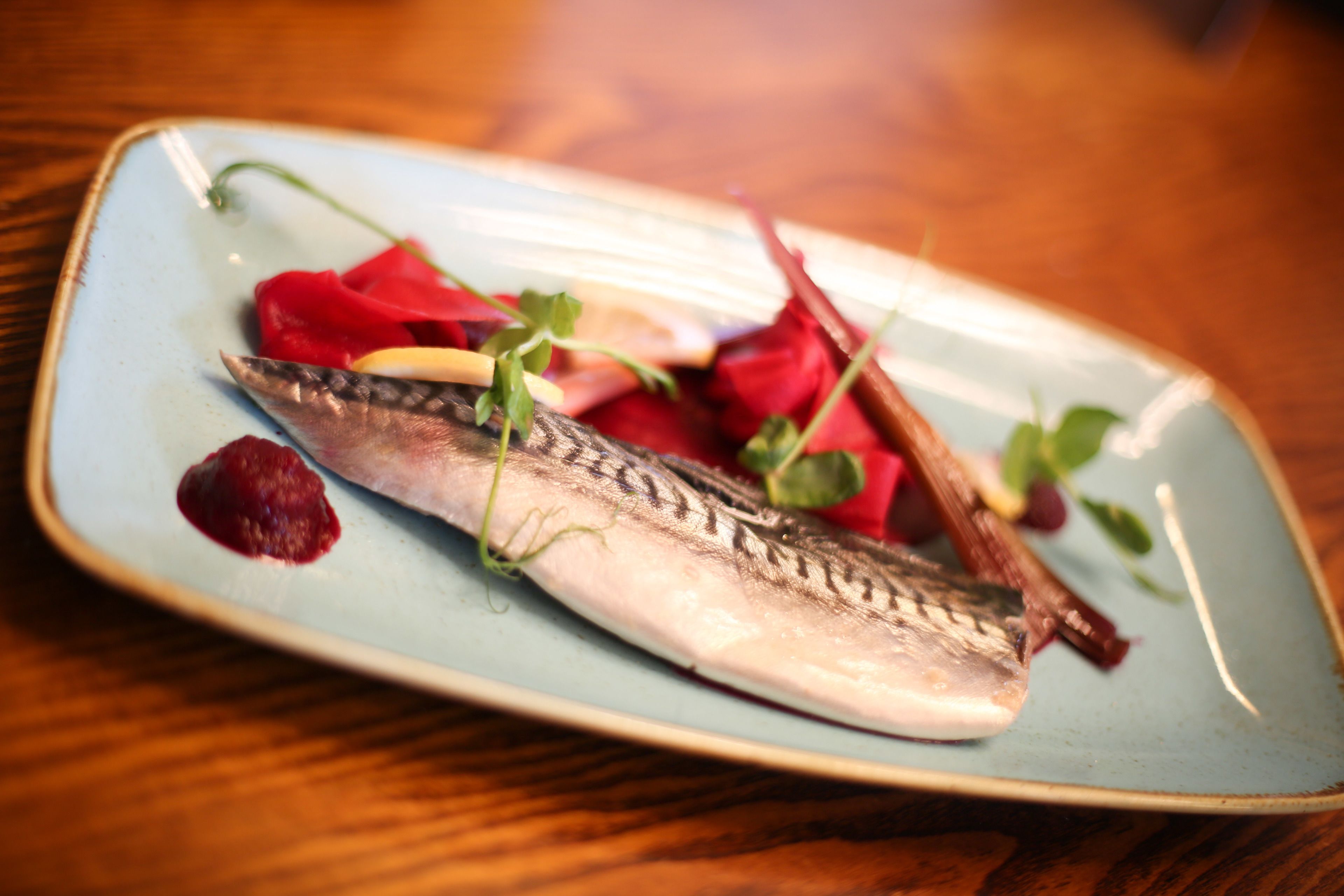 Um prato com peixe, vegetais vermelhos e ervas.