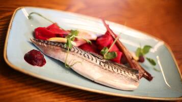 Um prato com peixe, vegetais vermelhos e ervas.