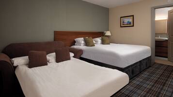 Quarto de hotel com duas camas, cabeceira de madeira, um quadro na parede e um banheiro visível através de uma porta aberta.