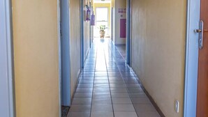Um corredor comprido e estreito, com pisos ladrilhados e portas em ambos os lados.