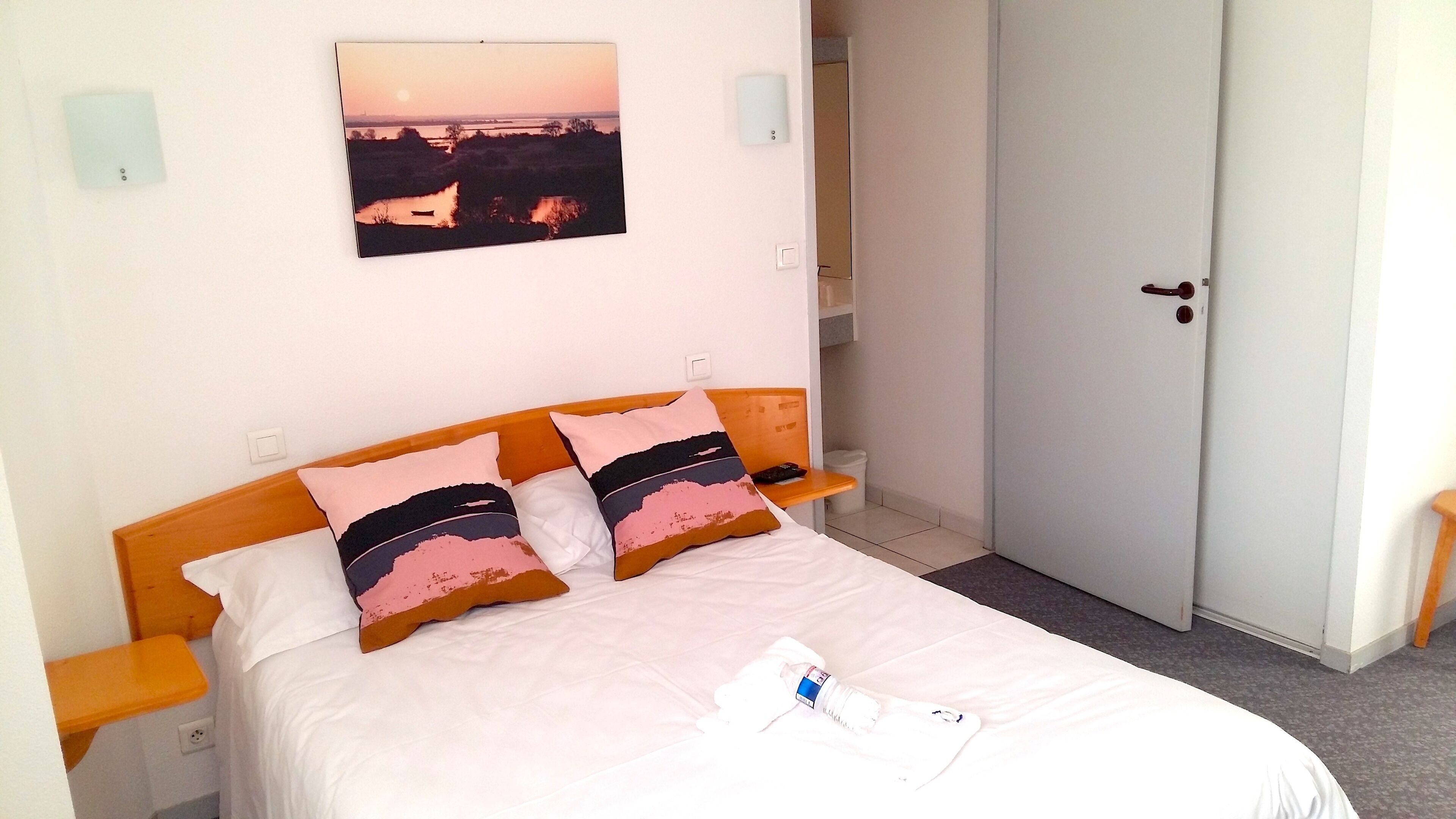 Quarto de hotel com cama, duas almofadas, mesa de cabeceira, guarda-roupa e um quadro na parede.