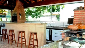 Cozinha com forno de tijolos, banquetas de madeira, bancada de granito e vista para o verde lá fora.