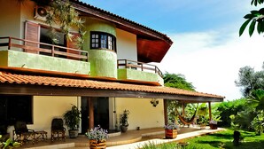 Uma casa de dois andares com varanda, plantas em vasos e uma rede.