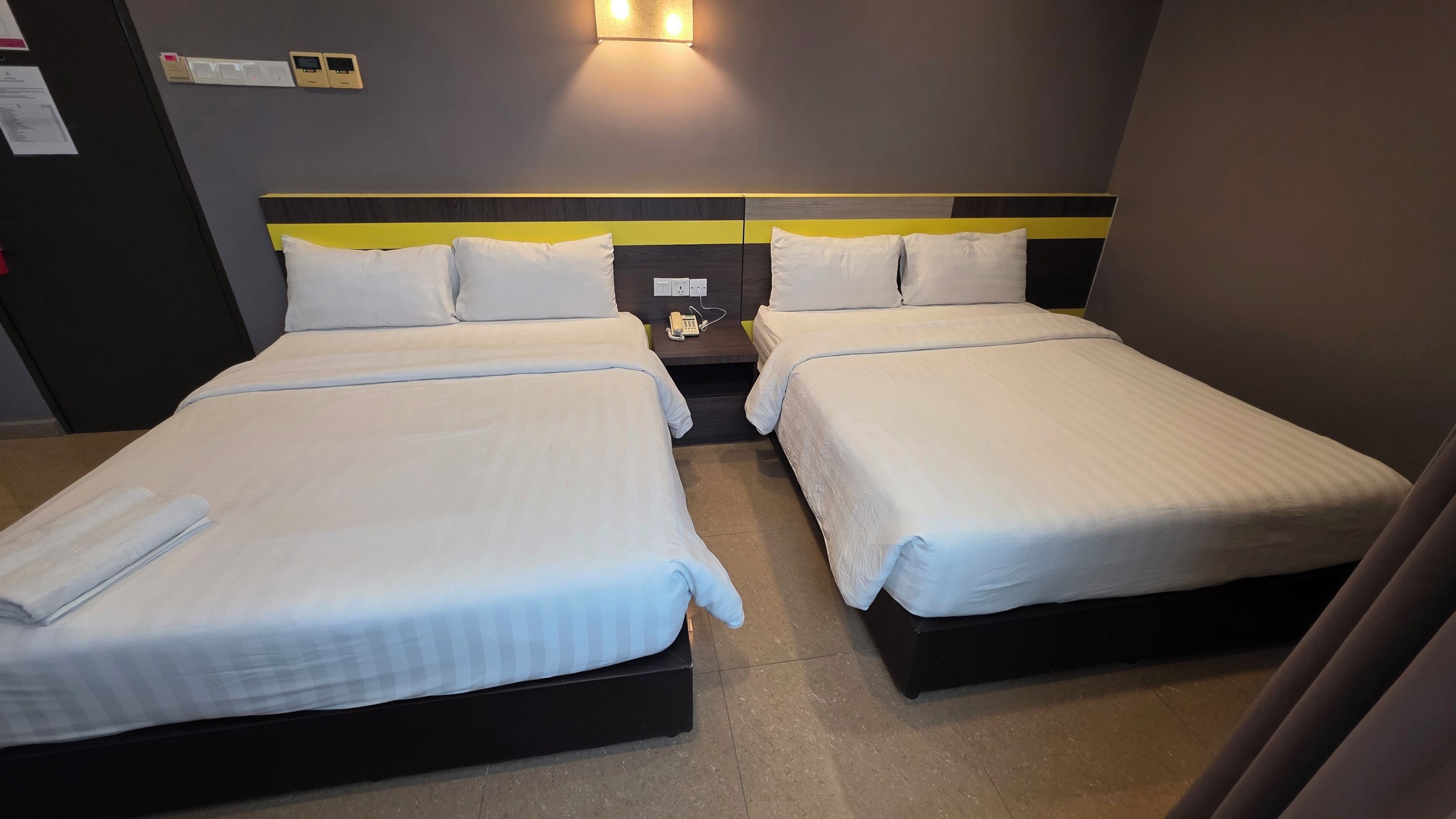 Quarto de hotel com duas camas, telefone ao lado da cama e luminária fixada na parede.