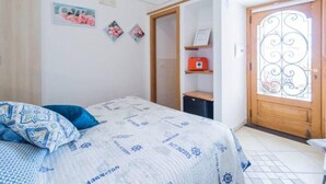 Um quarto com cama, guarda-roupa, prateleira com uma caixa vermelha e porta decorativa.