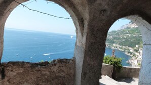 Estrutura de pedra em arco com vista para o mar e uma cidade distante.