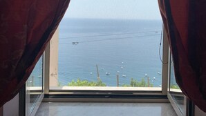 Quarto com grande janela com vista para o mar, mostrando barcos e um céu limpo.