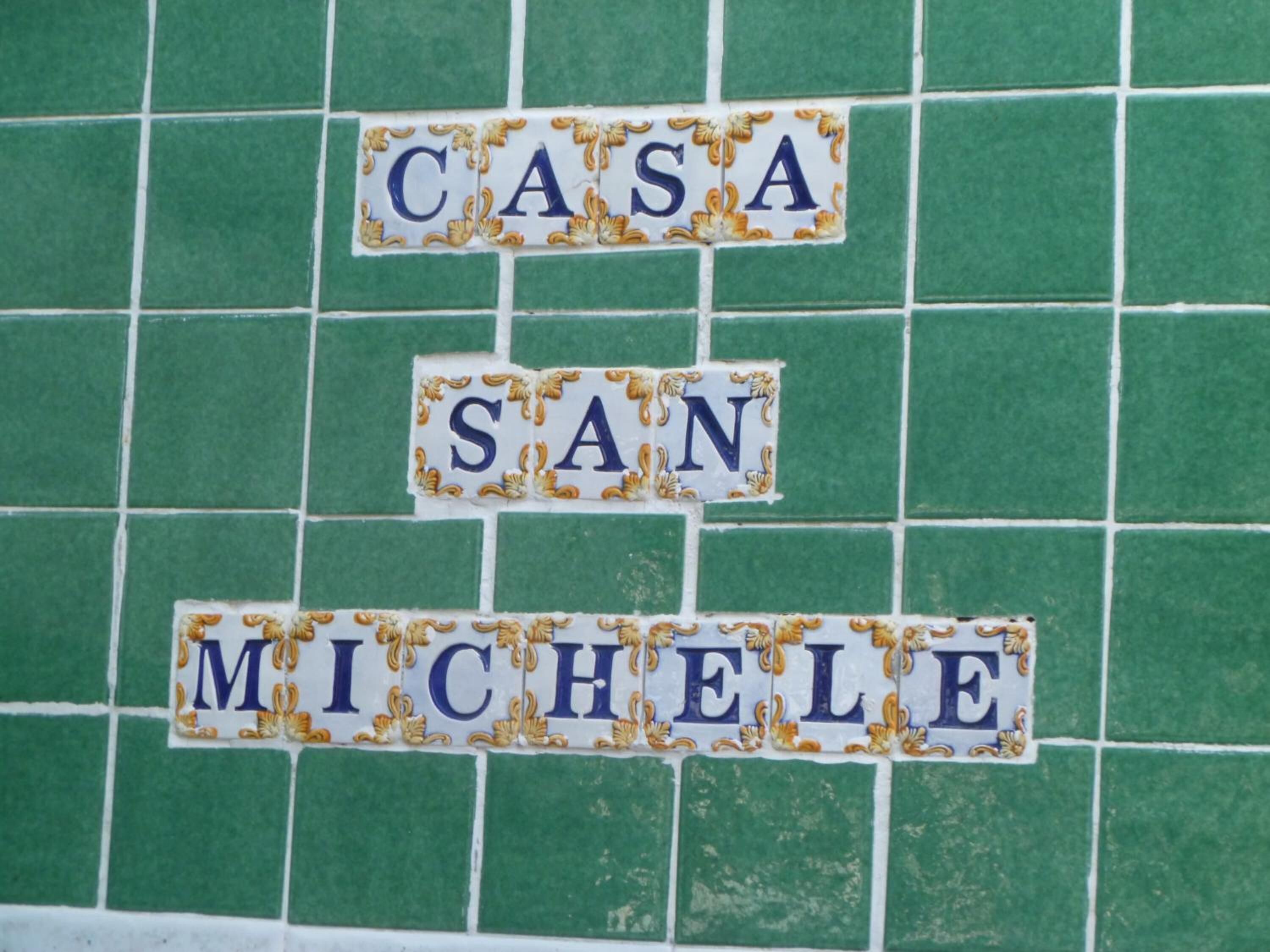 Parede revestida de azulejos com a inscrição "CASA SAN MICHELE" em azulejos decorativos.